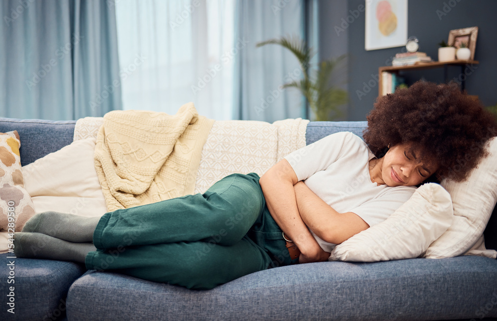 Black woman, lying on sofa with stomach, menstruation or pain holding ...