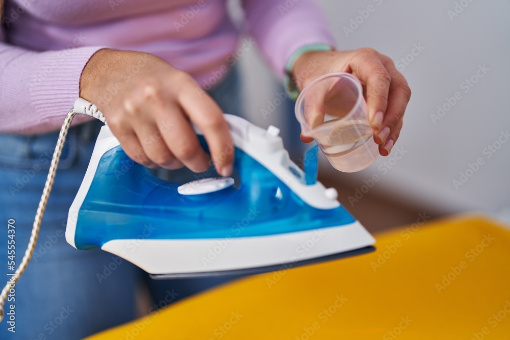 Young hispanic woman pouring water on iron machine at laundry room ...