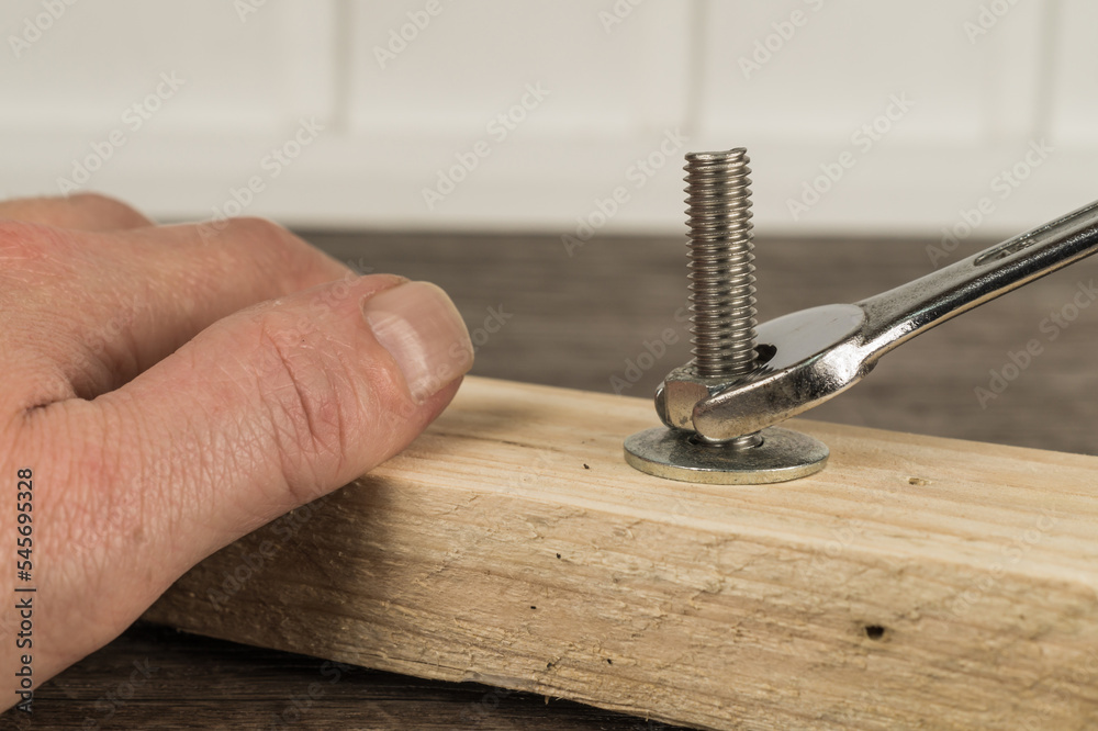 Hand holding piece of wood and metal wrench to tighten a nut and screw ...