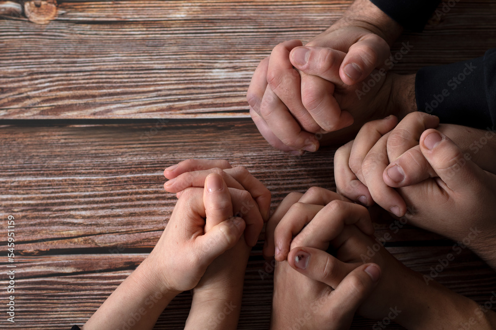 Praying hands on a wooden background with copy space. Top table view. Young Christian friends ...