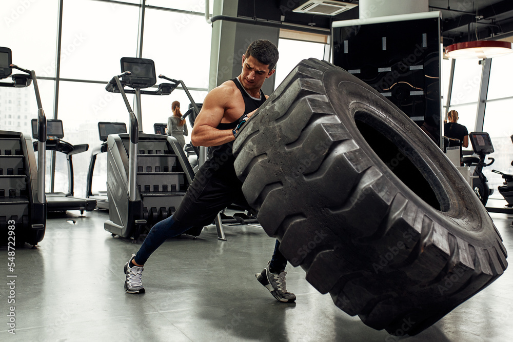 Muscular fitness man moving large tire in gym center, concept lifting ...