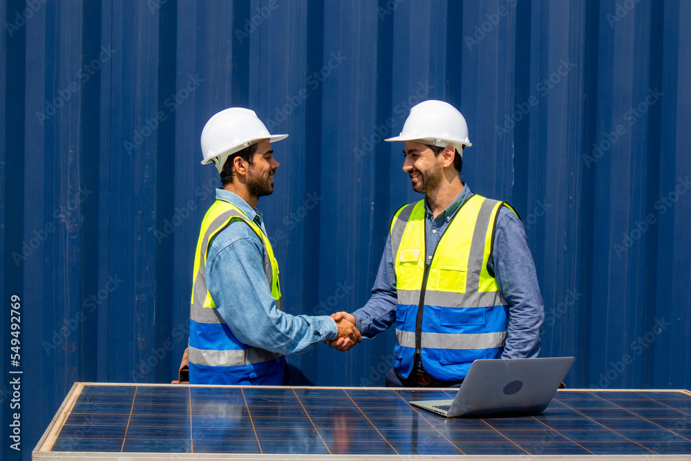 Two professional male engineers in helmets and uniforms shaking hands ...