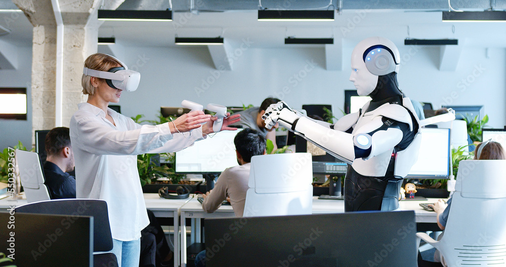 Woman in headset programming robot with metaverse tools. Developer in VR checking work of cyborg ...
