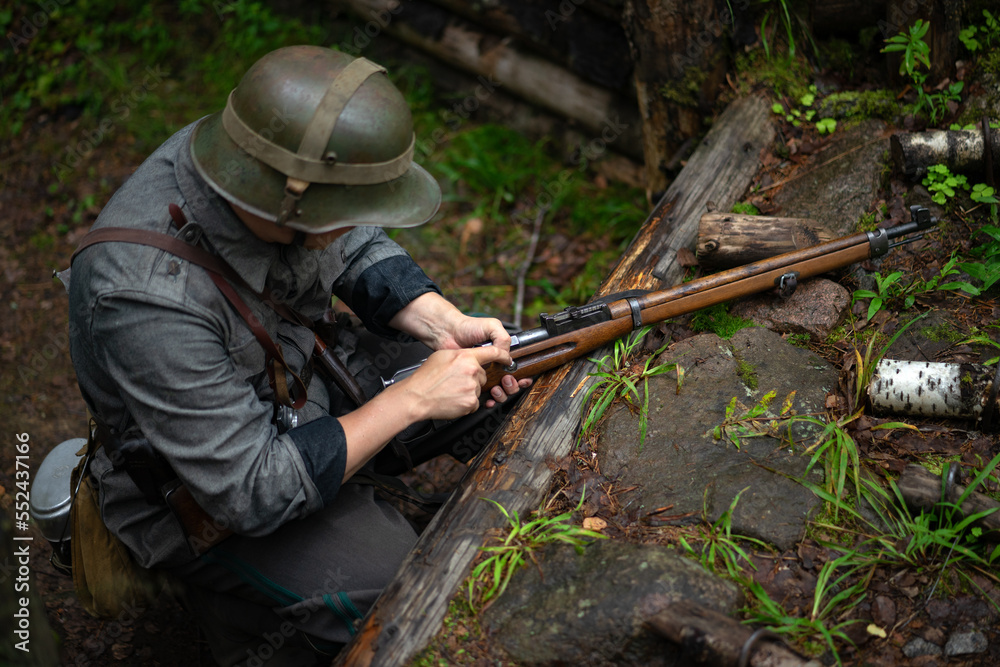 A soldier in a World War II uniform, reloading a rifle in a forest ...