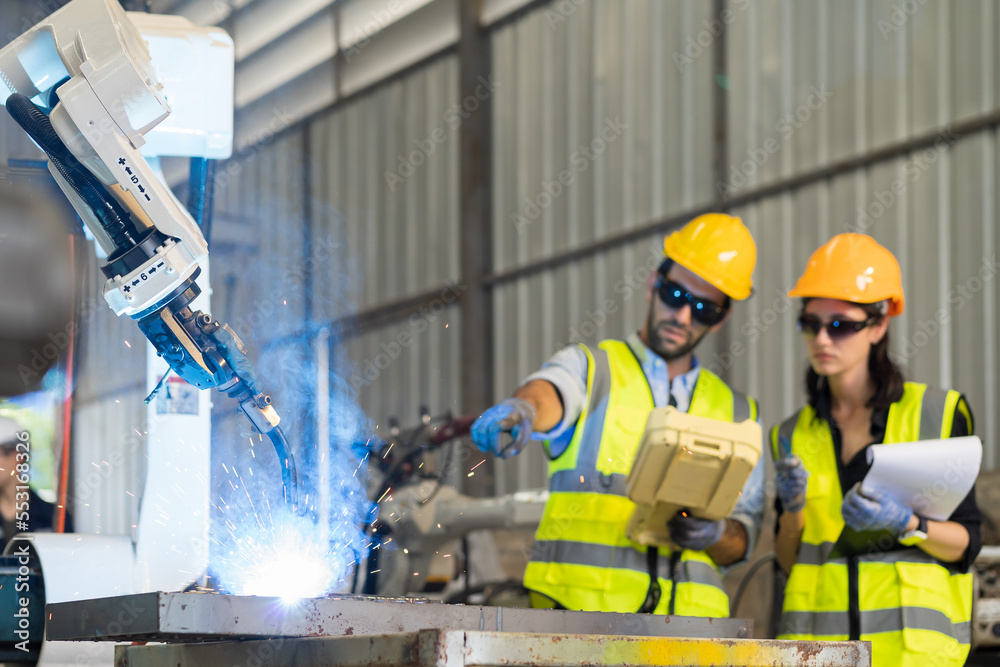 Two male and female engineer working with robot arm system welding at ...