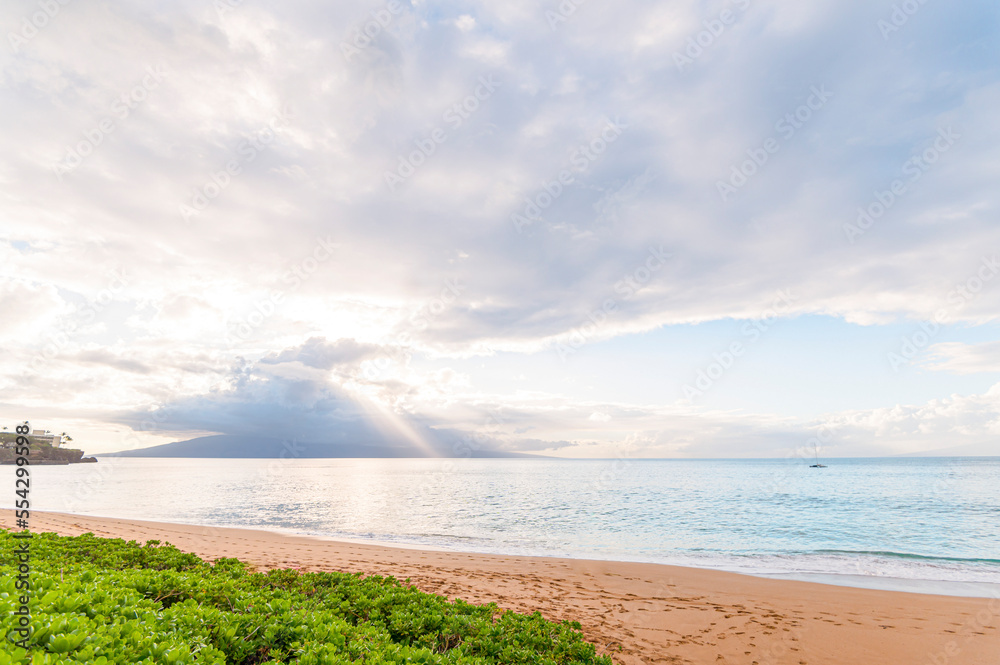Sun beams through the clouds and the calm shore at Kaanapali Beach in ...