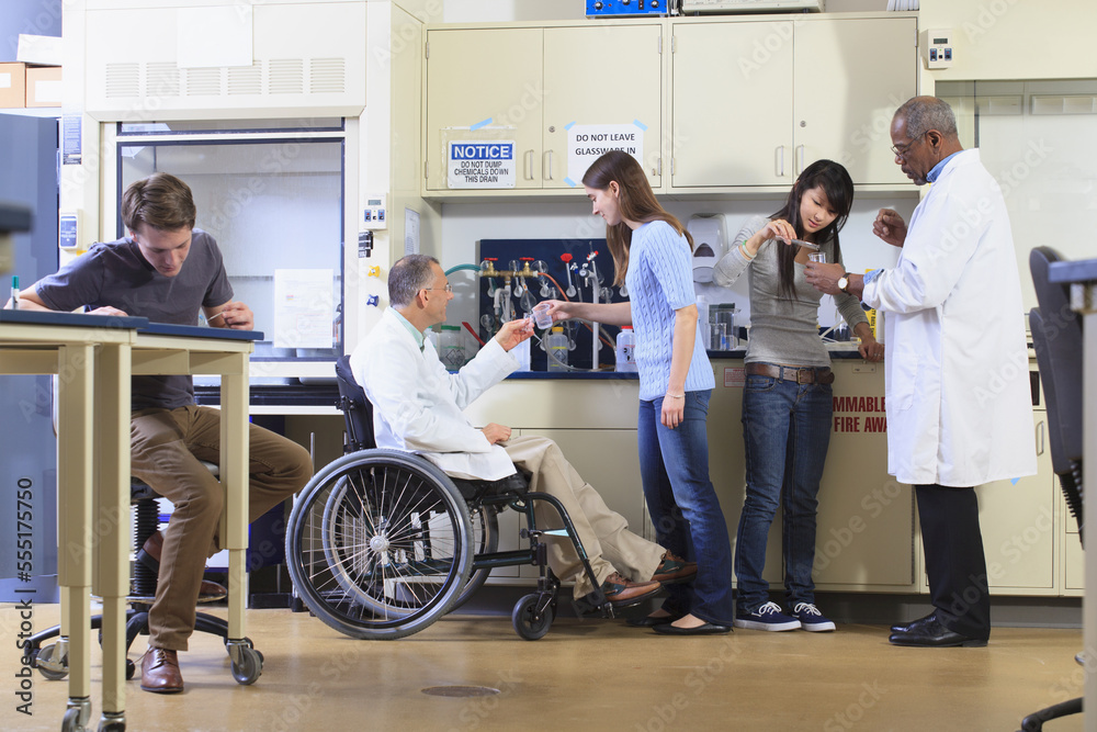 Two professors working with students in an engineering lab working on ...