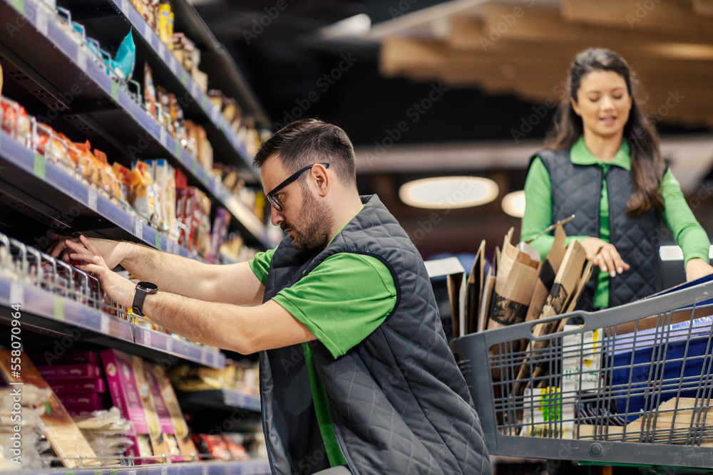 A supermarket worker is displaying groceries on shelves at marketplace ...