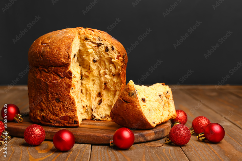 Board with cut Panettone and Christmas balls on table against black ...