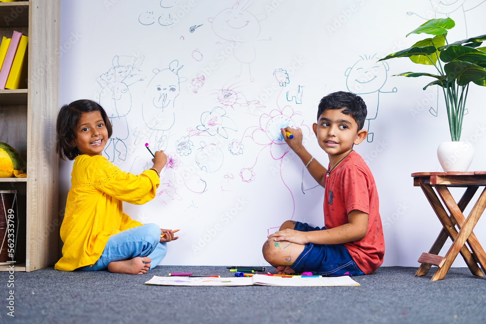 Young siblings kids drawing with crayon color on wall by looking at ...