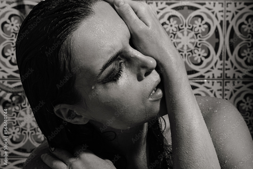 Sad and wet woman with smudged makeup on her face under the shower ...