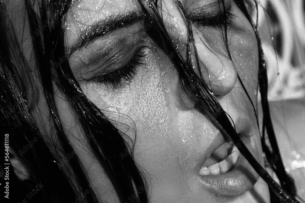 Sad and wet woman with smudged makeup on her face under the shower ...