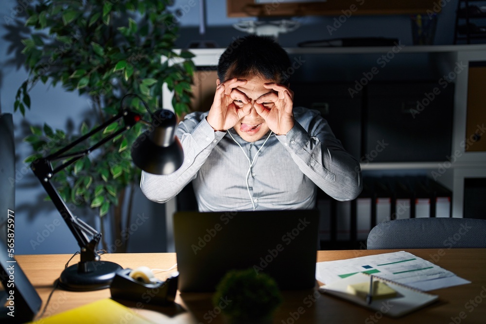 Young chinese man working using computer laptop at night doing ok ...