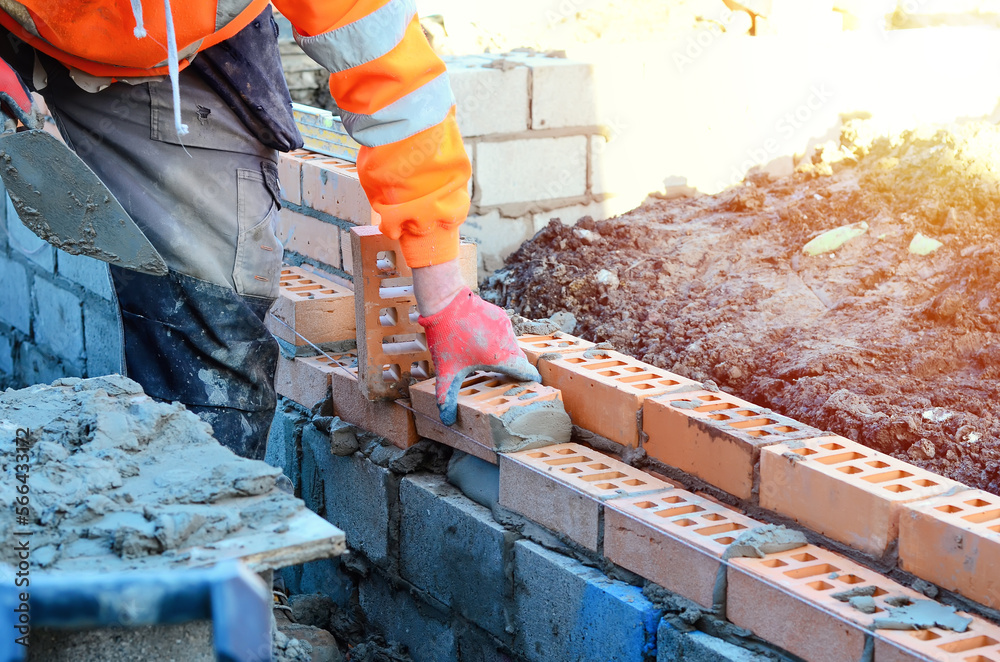 Industrial bricklayer laying bricks on cement mix on construction site ...