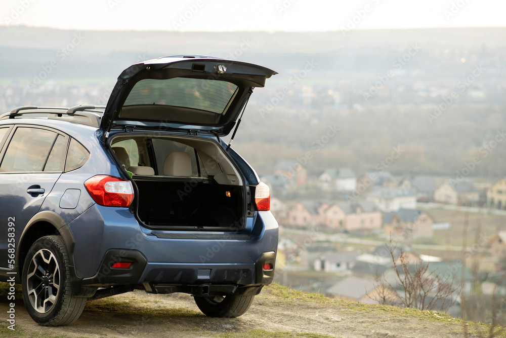 Blue off road car with open trunk lid at dawn on grassy hill on distant ...