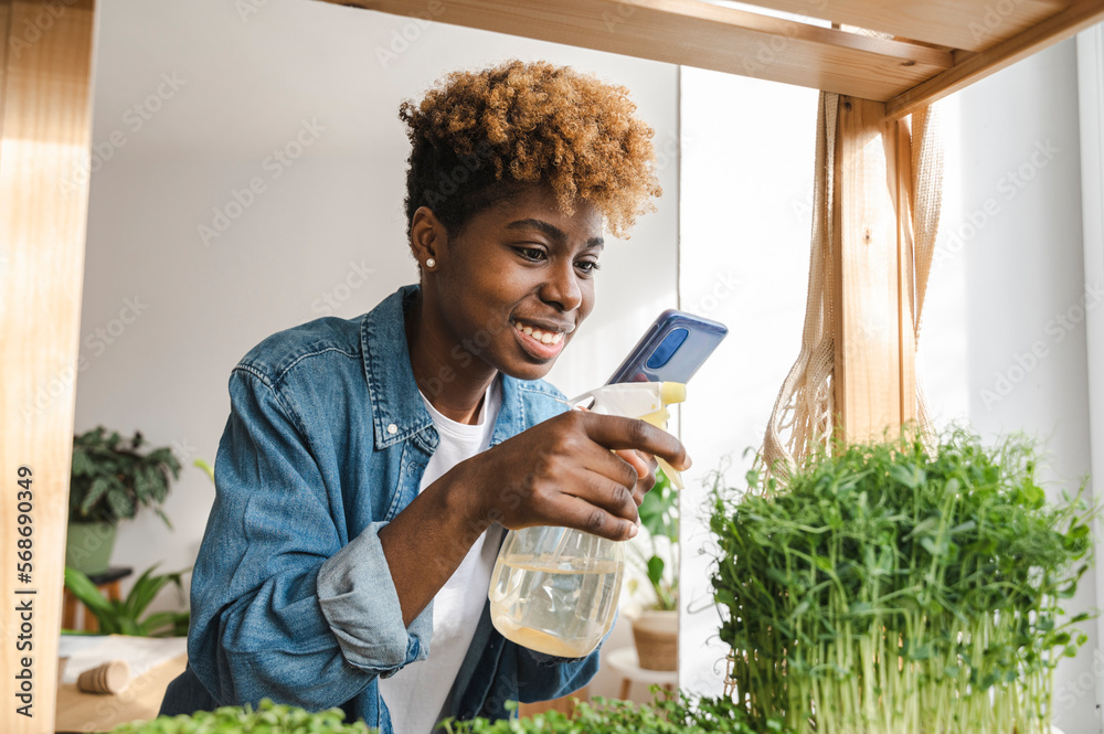 Smiling influencer spraying water on plants and vlogging over mobile ...
