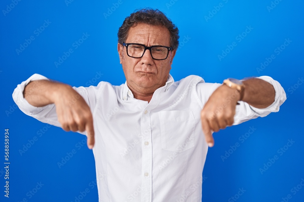Middle age hispanic man standing over blue background pointing down ...