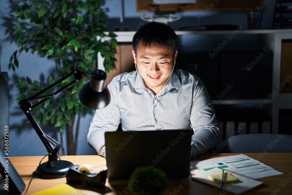 Young chinese man working using computer laptop at night with a happy ...
