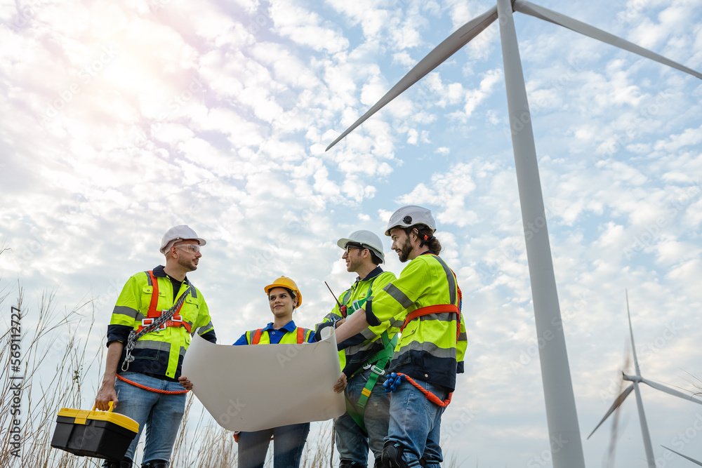Teamwork engineer worker wearing safety uniform holding and reading blueprint at wind turbine ...