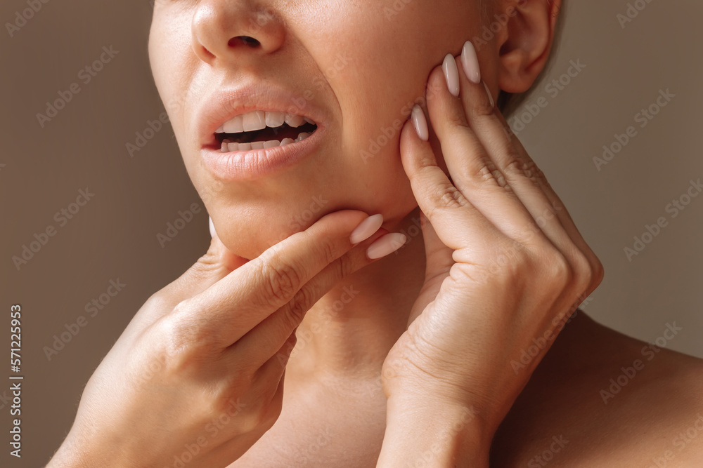 Cropped shot of young woman suffering from jaw pain holding her chin ...