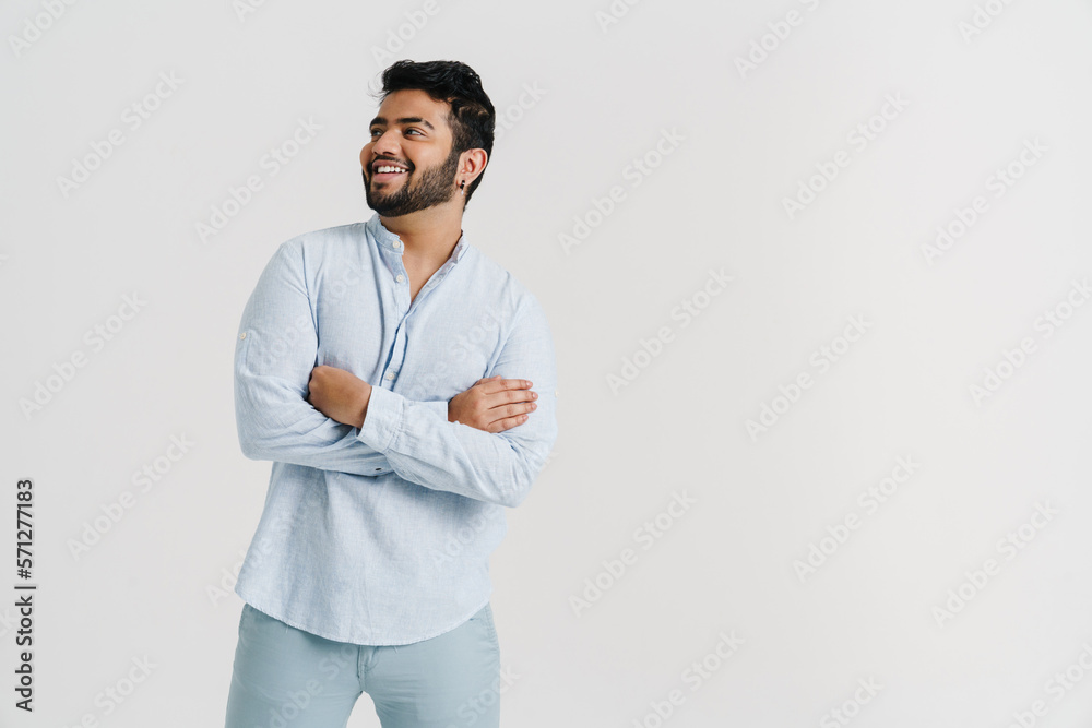 Smiling indian guy standing with arms folded isolated over white wall ...