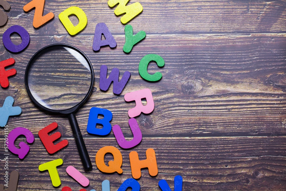 Multicolored English letters spread on the wooden floor. Magnifier and ...