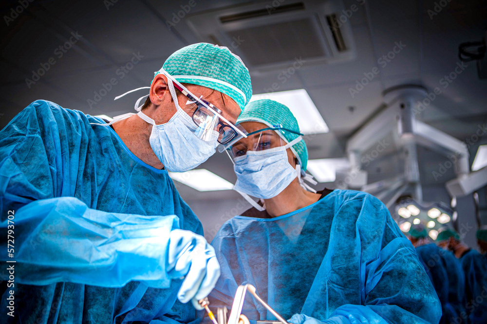 Two surgical residents holding retractors and scalpels during a ...