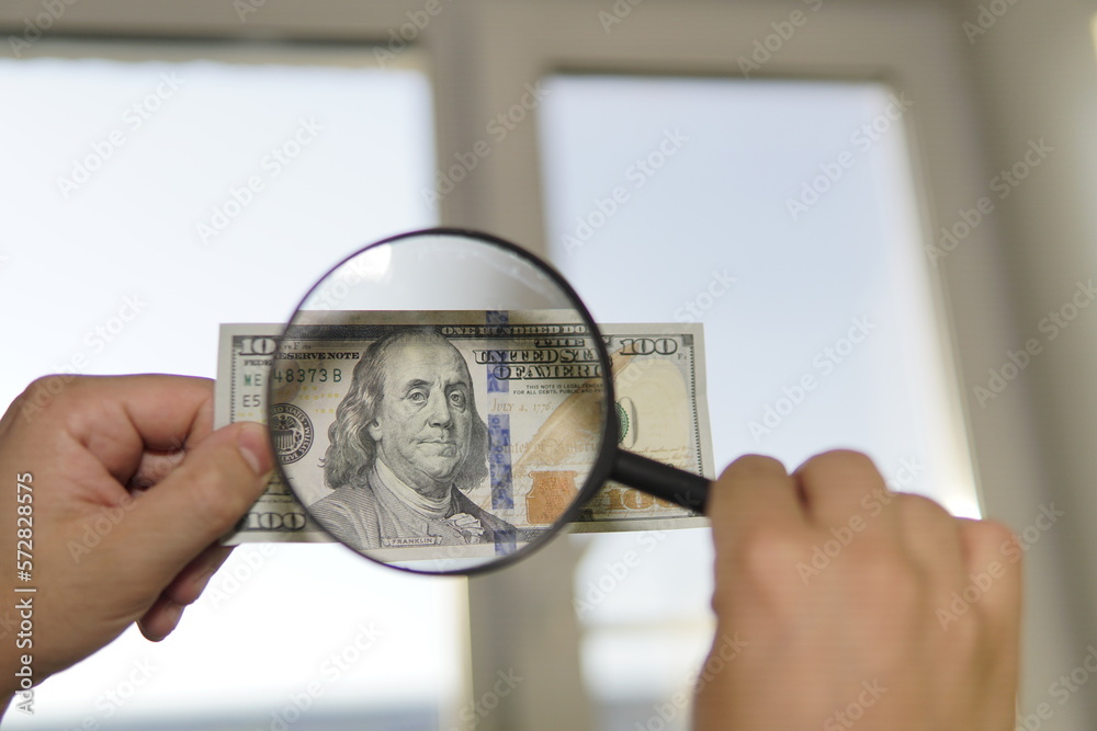 Checking counterfeit money light. 100 dollars against the window in his ...