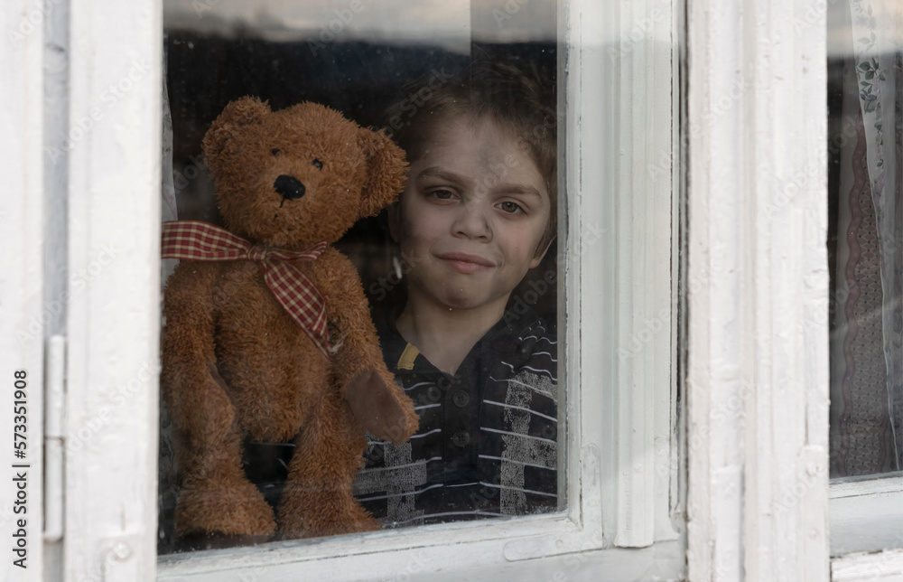 Little grimy boy looking through a dirty old window. A sad smile on his ...