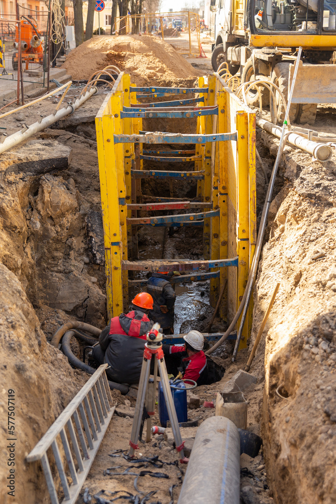Workers working at deepening supported by trench box with pipe bedding ...