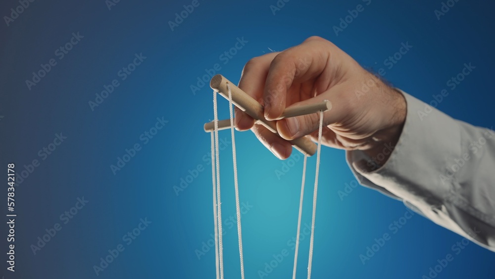 The hand of a man in a gray shirt controls a puppet using a wooden ...