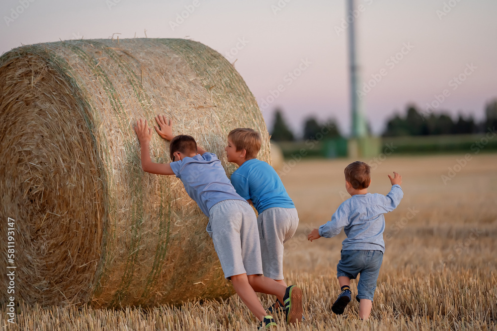 Children play in the green field with hay rolls in front of wind ...