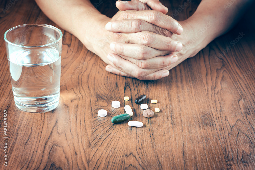 man holding tight hands together with a pile of pills and tablets in ...