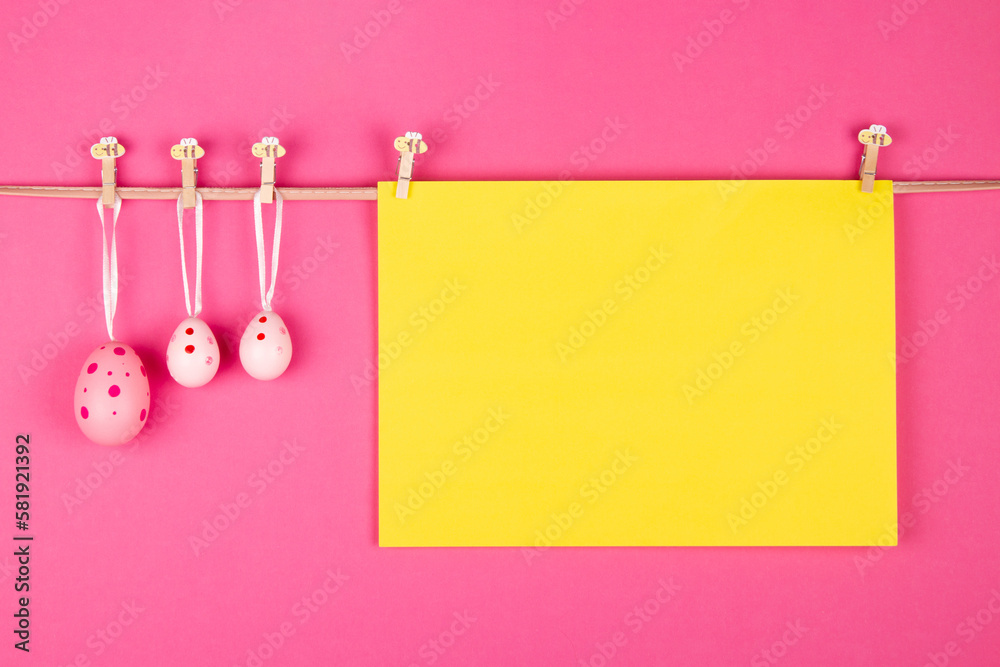 Blank yellow sheet of paper and three pink Easter eggs hang at rope on ...