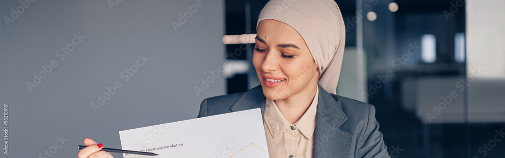 Smiling muslim businesswoman in hijab shows a graph of company's profit ...
