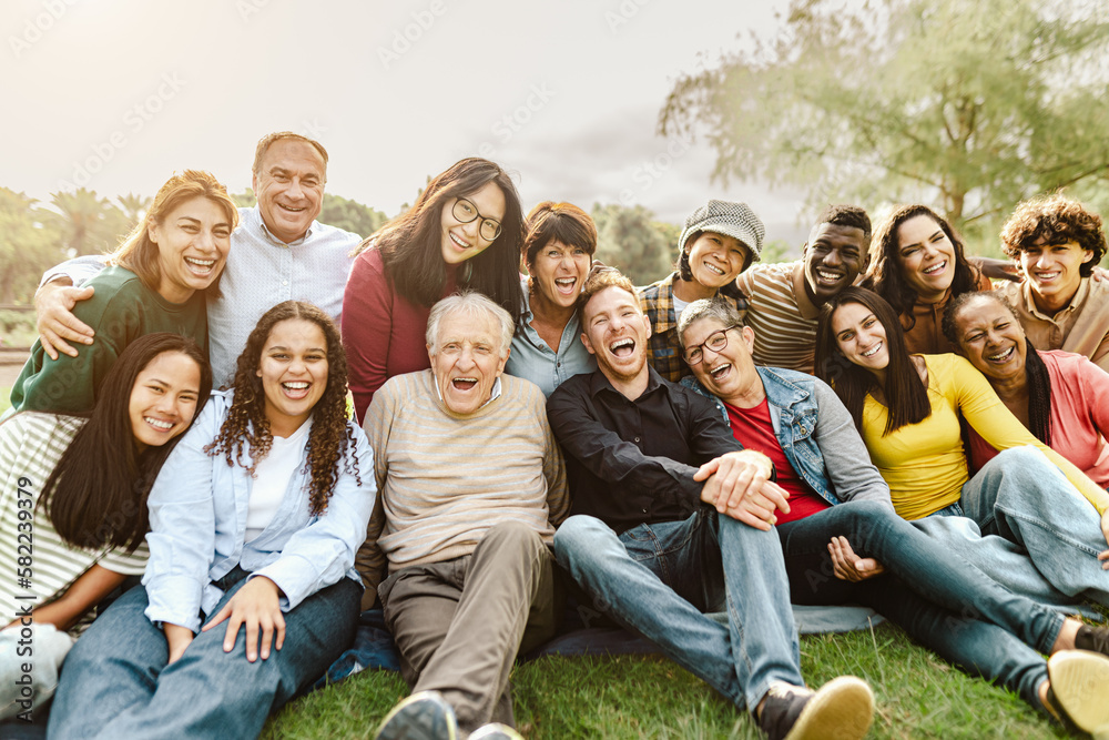 Happy multigenerational people having fun sitting on grass in a public ...