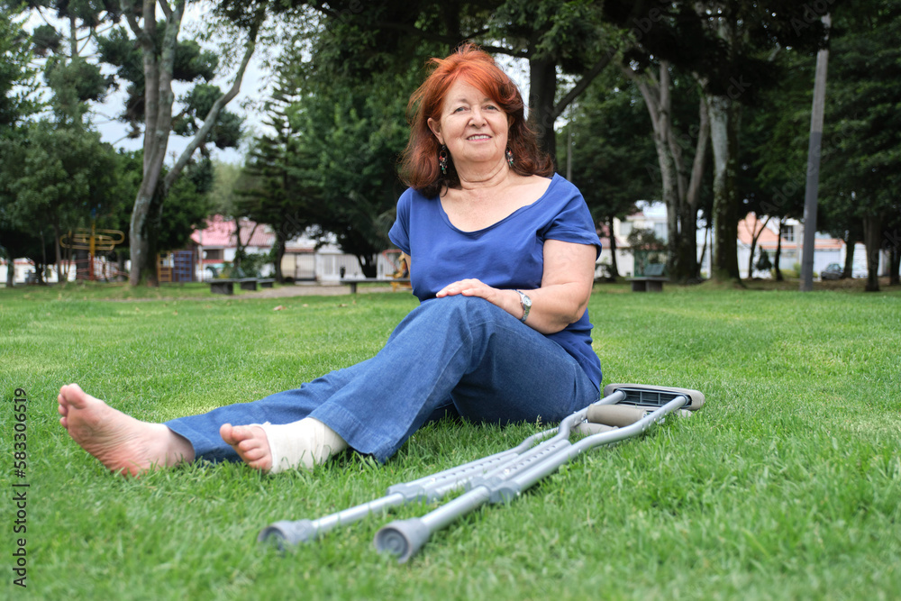 Mature woman resting on the grass, smiling, barefoot, with a bandage on ...