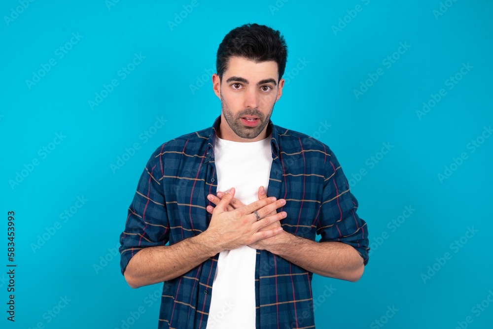 Scared Young man standing over blue studio background looks with ...