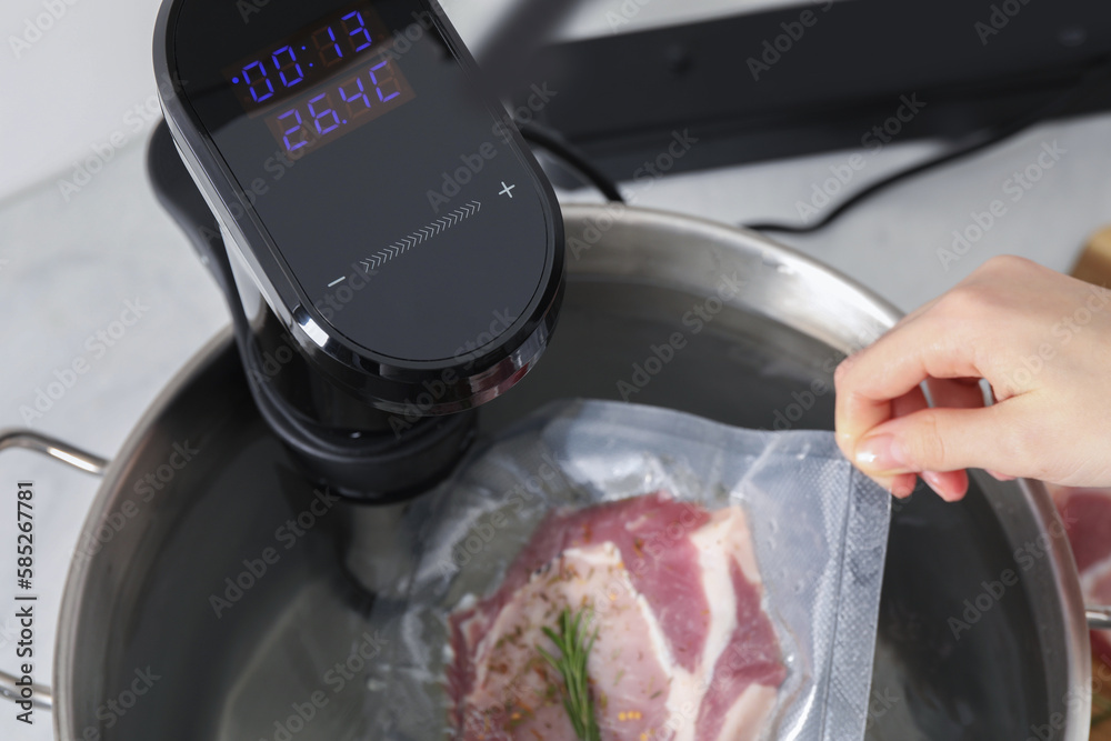 Woman putting vacuum packed meat into pot with sous vide cooker in ...