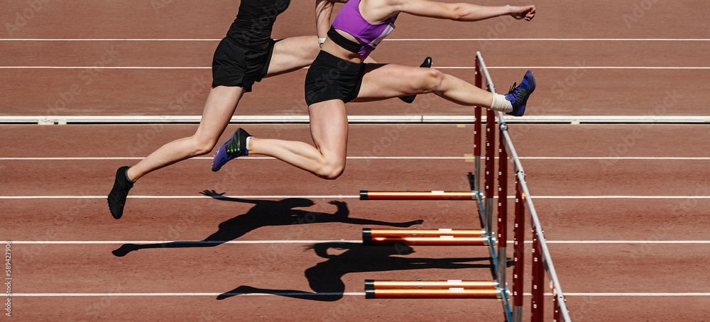 two female athletes running hurdles in athletics competition, hurdling ...