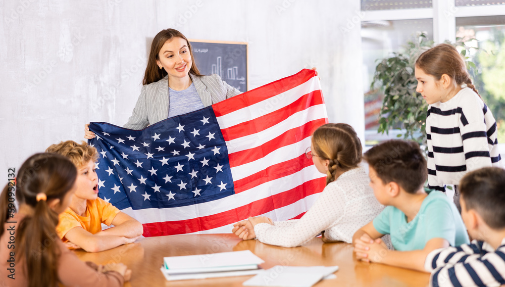 Smiling young woman teacher showing national flag of USA and telling ...