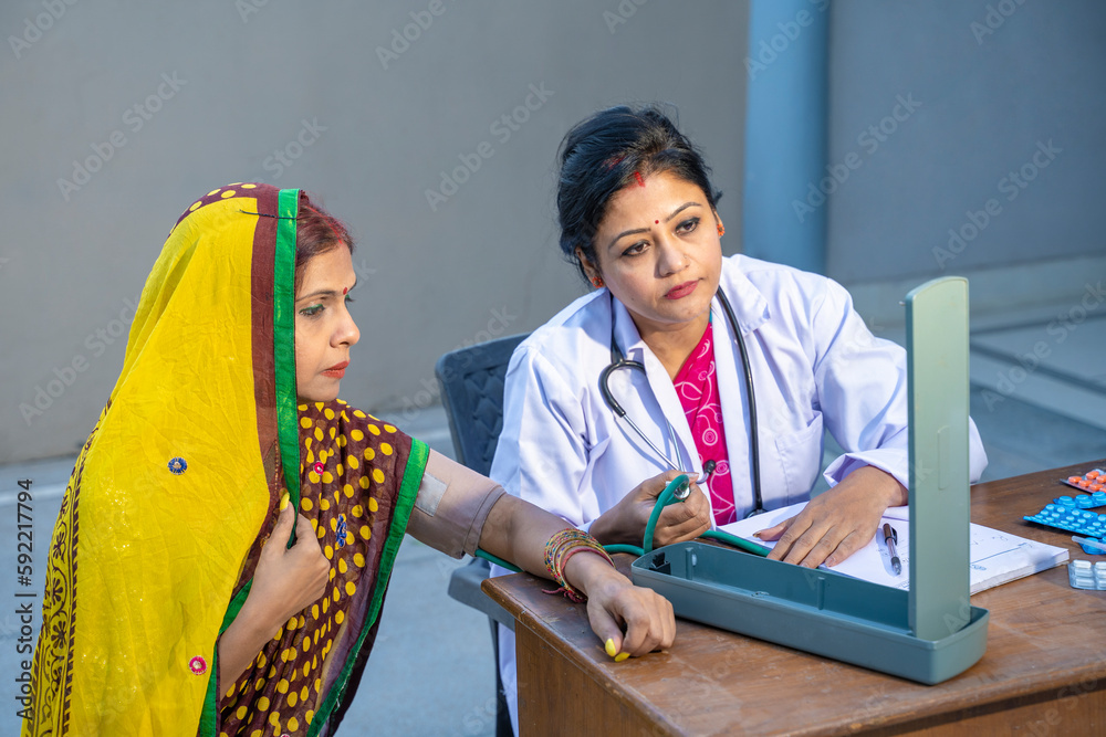 Indian female doctor checking blood pressure of rural woman at clinic ...