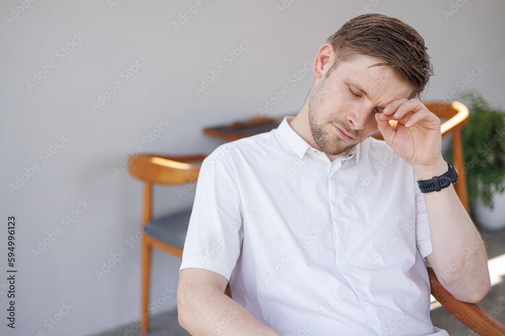 A tired man in a white shirt is sitting in a cafe. Summer heat ...