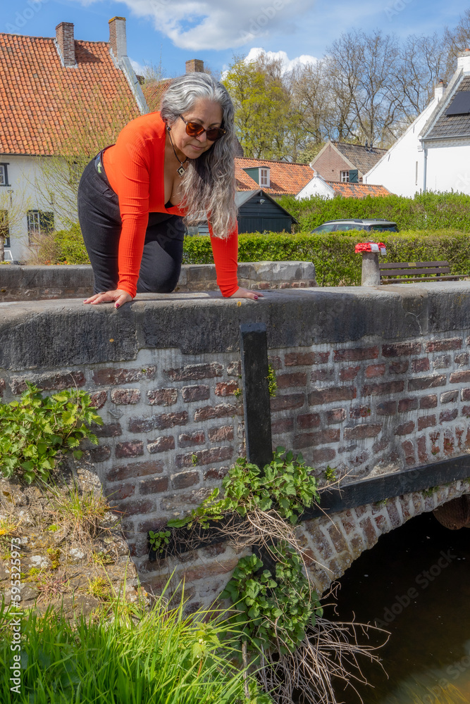 Latin American woman crouching and leaning over a bridge looking down ...