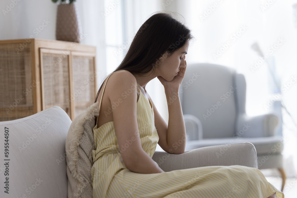 Tired unhappy late teenage girl sitting on home couch, touching face ...