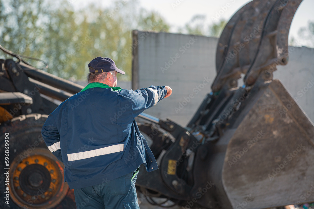 Male worker pointing on wheel loader and the garbage heap at a landfill ...