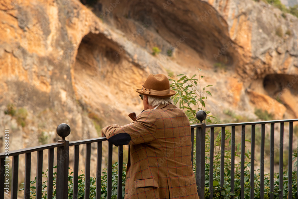 Older man with a pippe in profile with brown coat and hat leaning on a ...