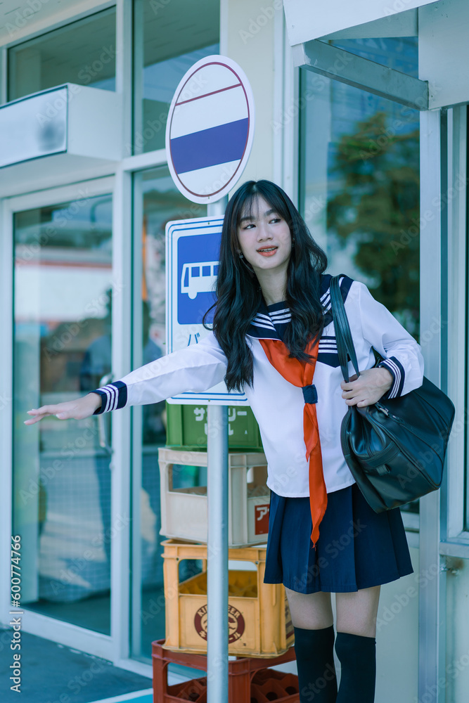 Cute Japanese schoolgirl in uniform downtown waiting at a bus station ...