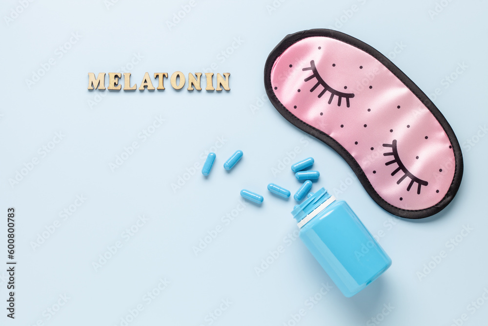 Blue bottle and pills, letters Melatonin and sleep mask on light grey ...