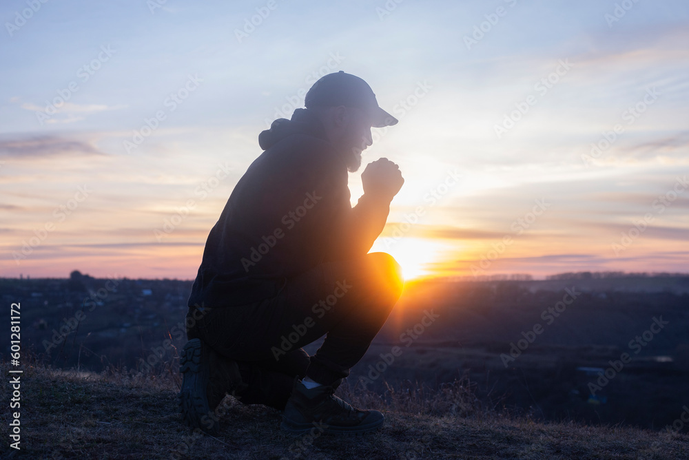 Man on his knees praying. On the background of the sunset sky. Kneeling ...